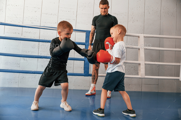 Fighting on the ring. Young tattooed coach teaching the kids boxing ...