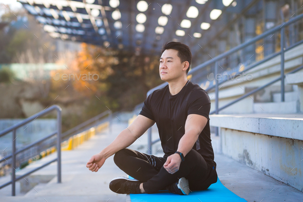 handsome asian man meditating in modern urban stadium, sitting lotus ...