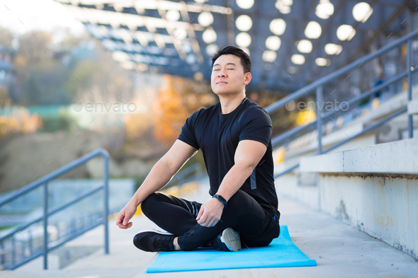 handsome asian man meditating in modern urban stadium, sitting lotus ...