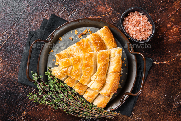 Slices of baked Round Borek cheese pie in kitchen tray with herbs. Dark ...