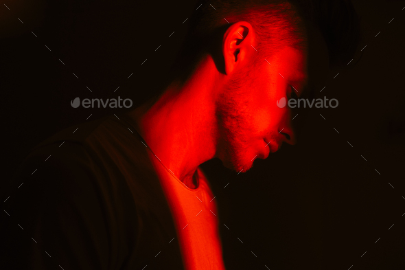 Side view portrait of caucasian young man in a dark with red light ...
