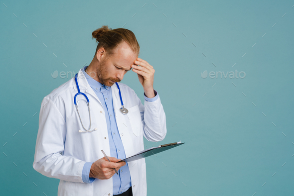 Puzzled male doctor wearing lab coat posing with clipboard Stock Photo ...