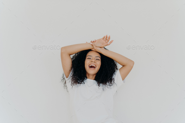 Overjoyed Curly Haired Young Lady Keeps Both Hands On Forehead Opens