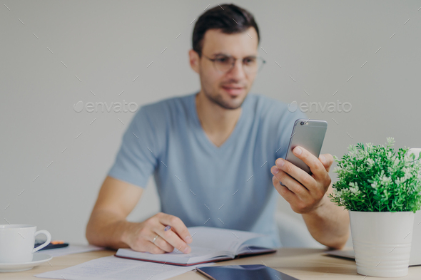 Busy male office worker recieves messages on mobile phone while makes ...