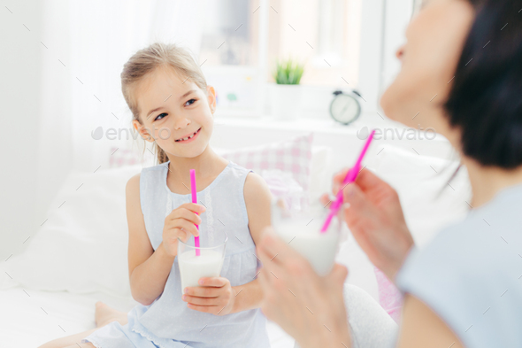 beautiful small female child drinks tasty milk shake together with her ...