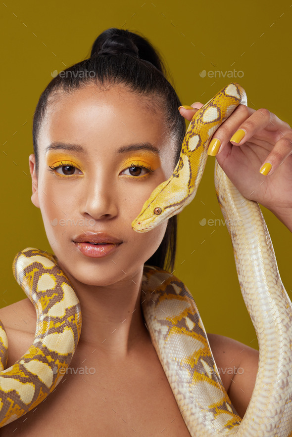 Shot of a young woman posing with a snake around her neck against a ...