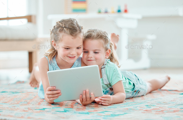 Shot of two adorable girls using a digital tablet while lying on the ...