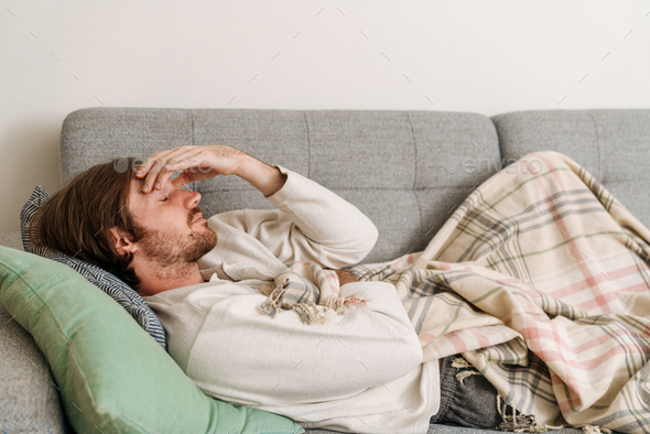 Ginger man feeling sick and covering his face while lying on couch ...