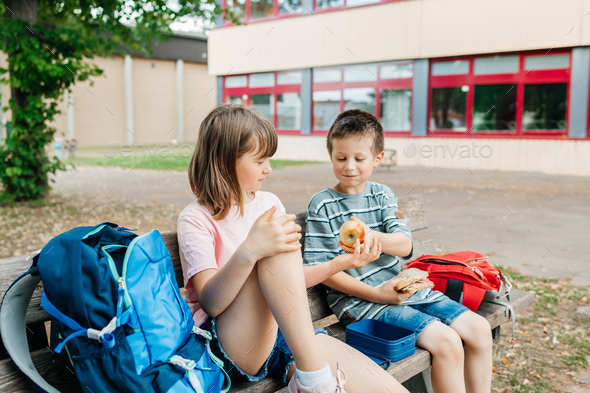 Children sit on a bench in the school yard and eat apples and ...