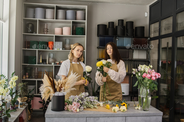 Two smiling florists in uniform work in a flower shop behind counter ...