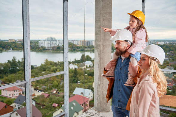 Happy family with child standing at construction site. Stock Photo by ...
