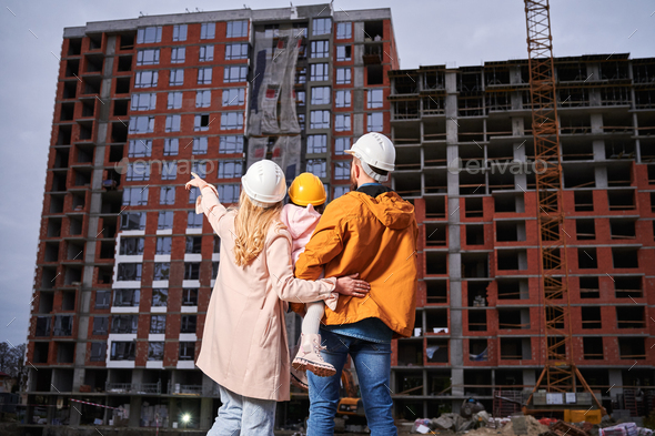 Family with child looking at apartment building under construction ...