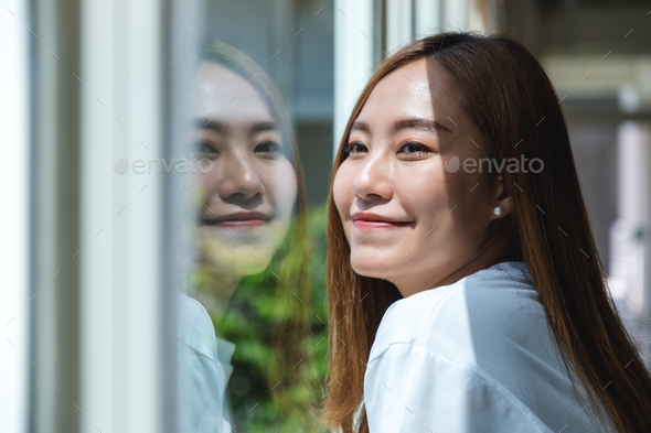 Portrait image of a beautiful young asian woman looking outside the window Stock Photo by Farknot