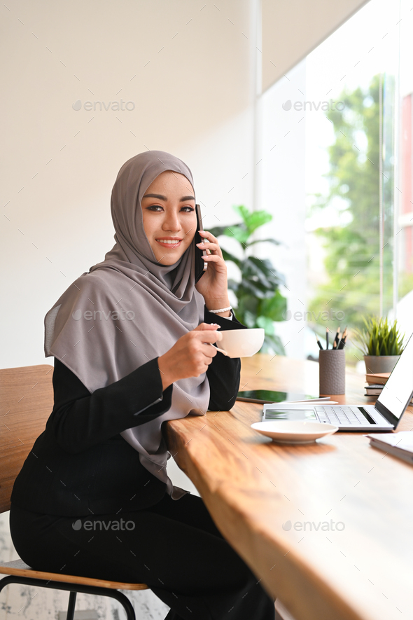 Smiling Muslim woman in hijab having pleasant phone conversation and ...