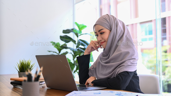 Beautiful young Muslim business woman in hijab sitting at modern office ...