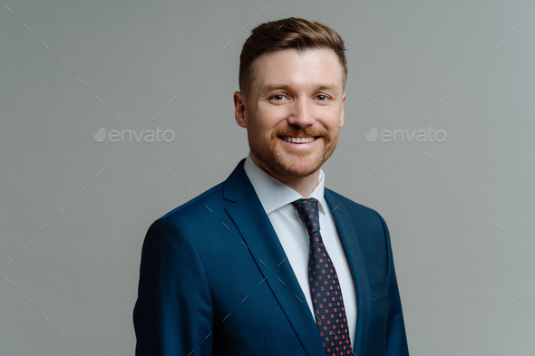 Cheerful male CEO in suit smiling at camera while posing against grey ...