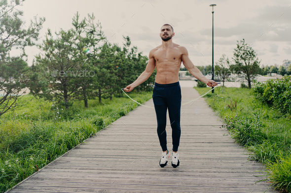 Sporty muscular man uses skipping rope for cardio training outdoor, has ...