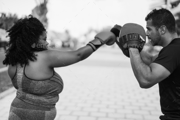 African curvy woman and personal trainer doing boxing workout session ...