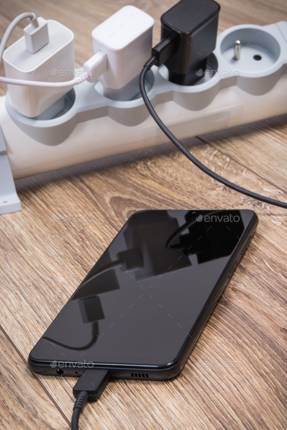 Smartphone and chargers connected to electrical power strip. Various ...