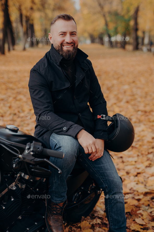 Vertical image of smiling motorcyclist smiles happily, holds helmet ...