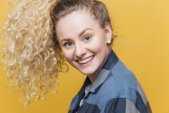 Sideways shot of pleased adorable young female model with curly hair ...
