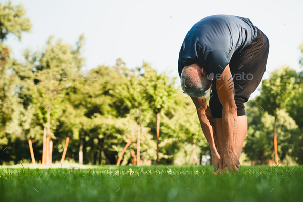 Man bending during stretching exercises on yoga mat in public park ...
