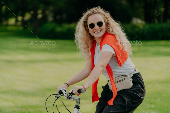 Photo of curly European woman keeps hands on handlebar of bicycle Stock ...