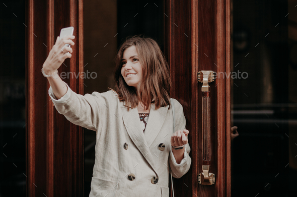 Adorable female student poses for making selfie, uses modern cell phone ...