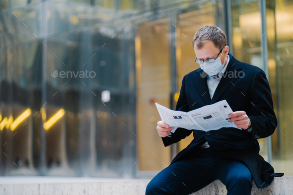 Outdoor shot of serious man boss takes break after walking, reads ...