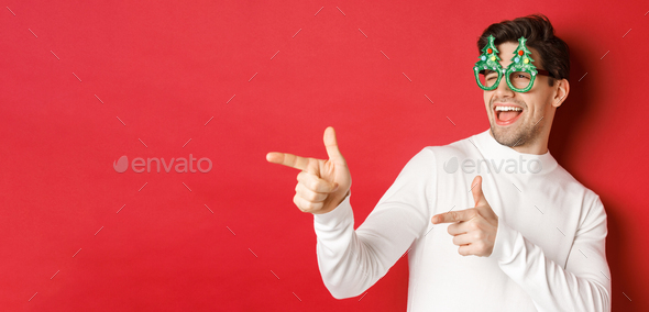 Close-up of cheeky handsome man in party glasses, pointing finger left ...