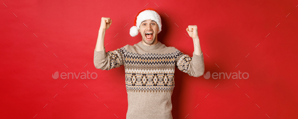 Image of cheerful handsome man in swearer and santa hat, celebrating ...