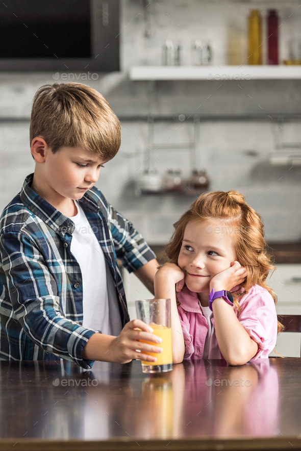 adorable little brother giving glass of orange juice to his smiling ...