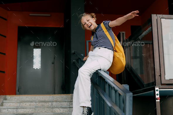 A teenage girl laughs and slides down the railing on her way to school ...