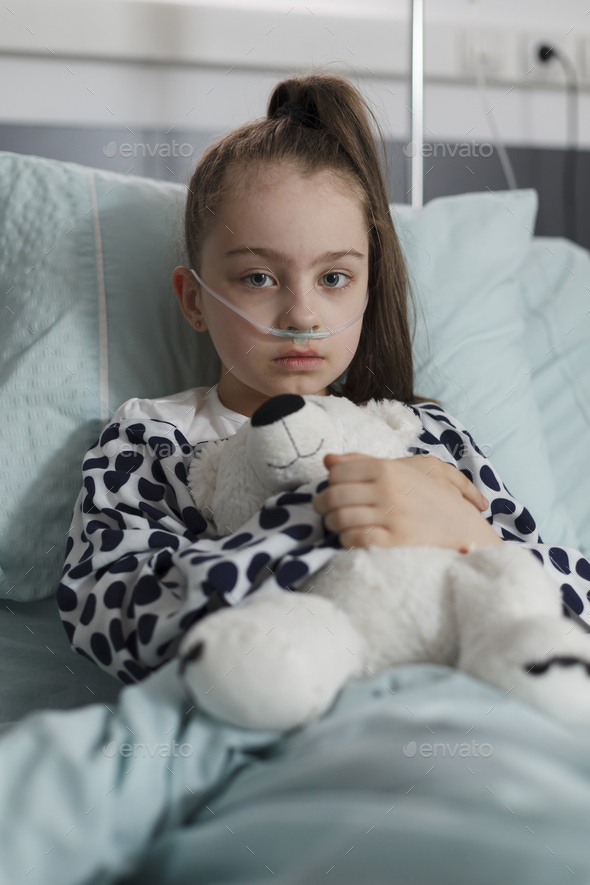Sick kid wearing oxygen tube while sitting in patient bed having plush ...