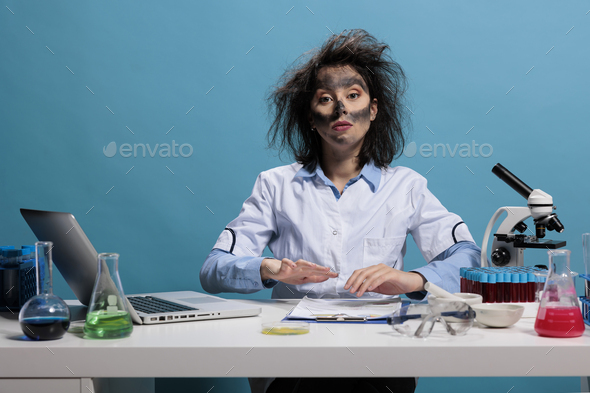 Mad silly looking scientist sitting at desk in laboratory with messy ...