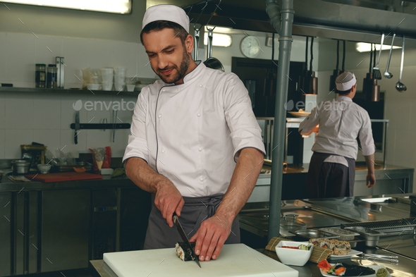 Smiling Male Chef in uniforms preparing sushi in a kitchen of asian ...