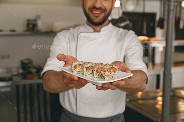 Handsome chef of japanies restaurant showing plate with sushi standing ...