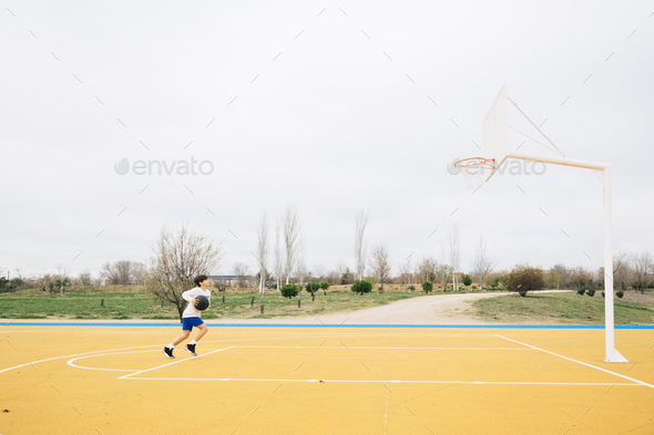 Young boy playing on yellow basketball court outdoor. Stock Photo by ...