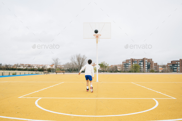 Young boy playing on yellow basketball court outdoor. Stock Photo by ...