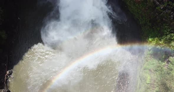 Drone rising and spinning above waterfall showing a rainbow as well ...