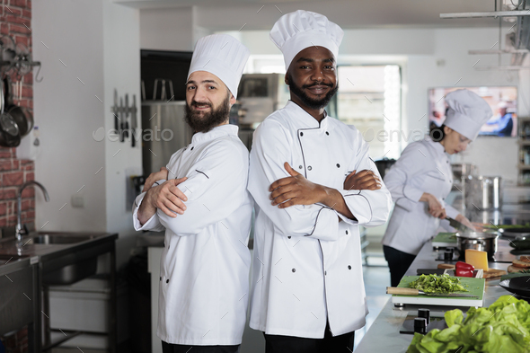 Confident smiling chefs standing in restaurant kitchen with arms ...