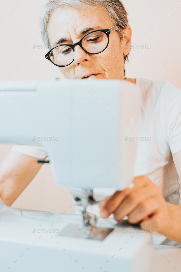 Old woman tailor working on sewing machine smiling happy to camera ...