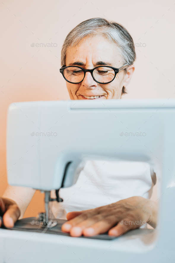 Old woman tailor working on sewing machine smiling happy to camera ...