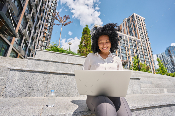 Smiling mixed race female sits with laptop on granite steps Stock Photo ...