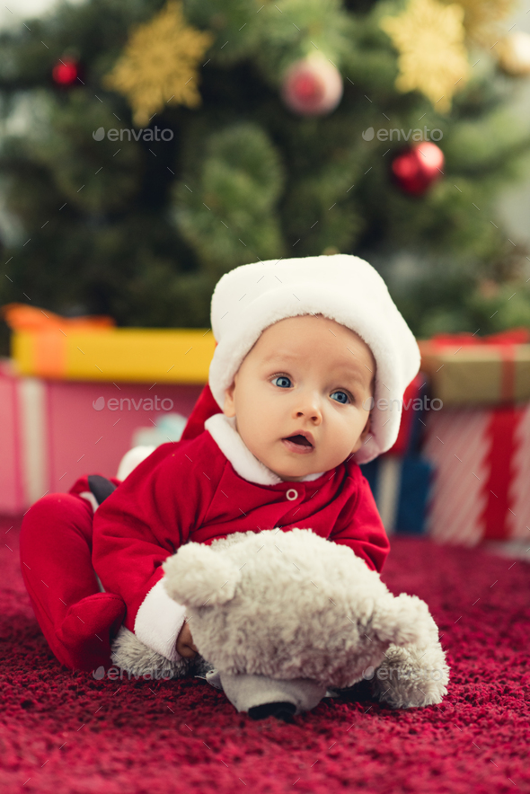 close-up portrait of cute little baby in santa suit lying on red carpet ...