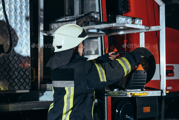 side view of female firefighter standing at equipment in truck at fire ...