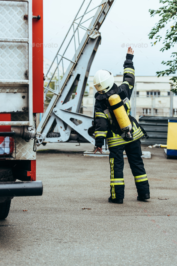 rear view of firefighter in uniform and helmet with fire extinguisher ...