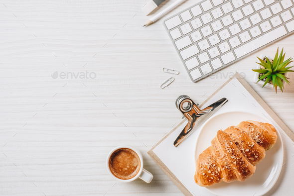 elevated view of clipboard, computer keyboard, croissant and coffee cup ...