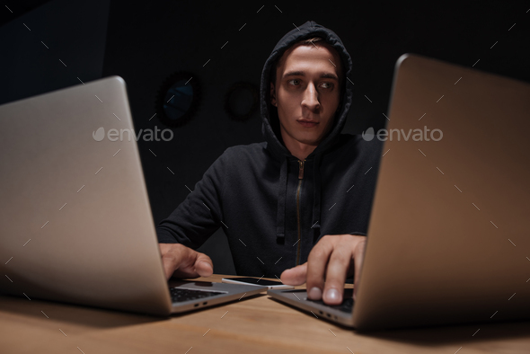 portrait of hacker in black hoodie using laptops in dark room, cyber ...
