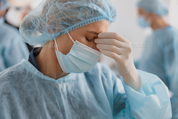 Professional tired surgeon in mask standing in operating room after ...